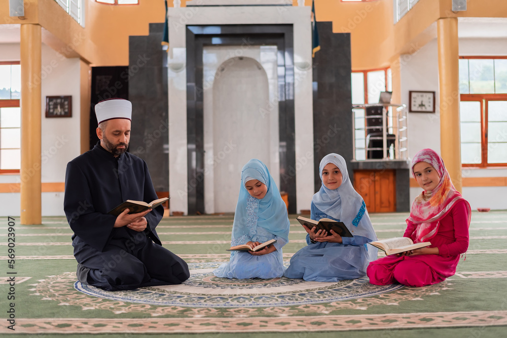 A Muslim teacher teaches children girls to read a holy book Quran ...