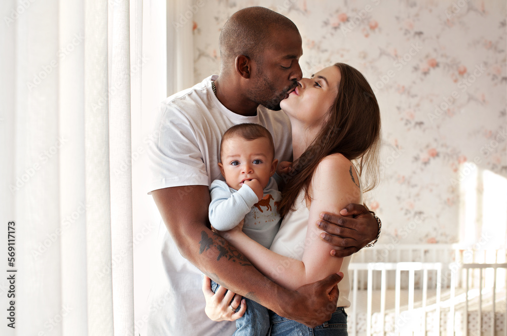 Happy multiethnic family hugging and kissing at home. Mom and Dad kiss ...