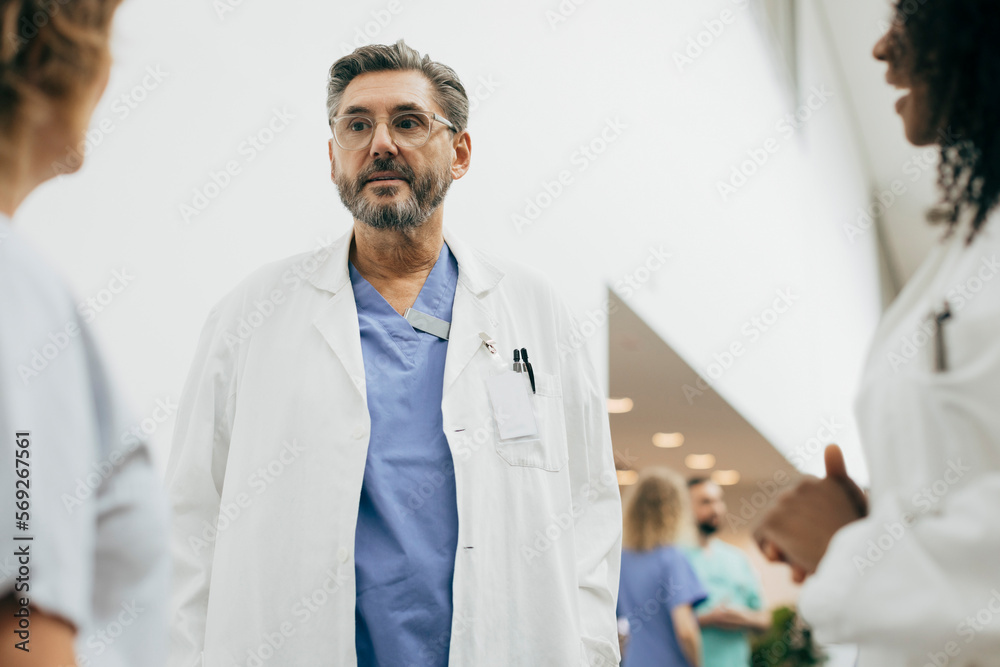 Mature male doctor wearing lab coat discussing with coworkers at ...
