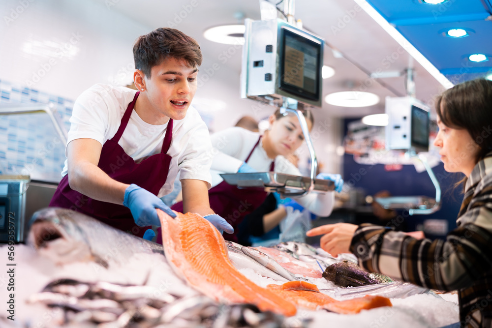 Positive young salesman demonstrating piece of salmon behind counter in ...