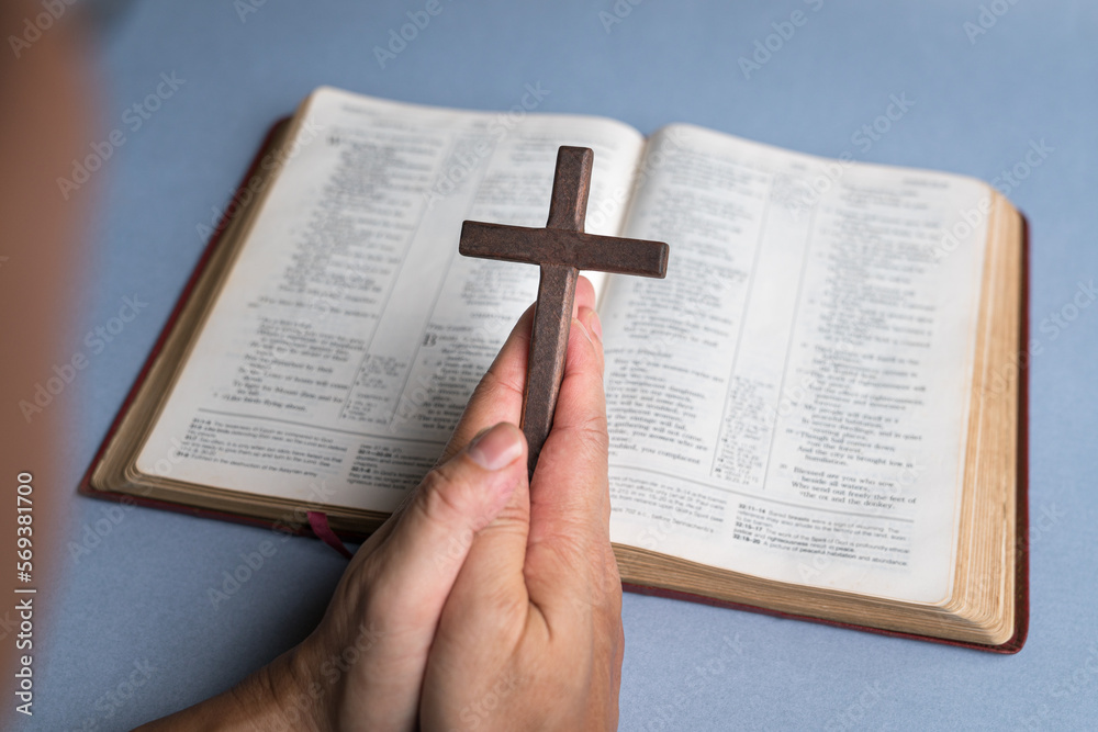 Man praying holding cross crucifx with open bible at the background ...