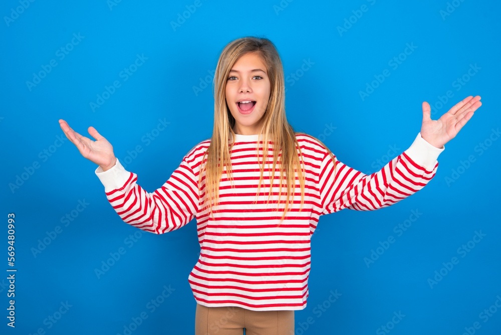 Cheerful caucasian teen girl wearing striped shirt over blue studio ...