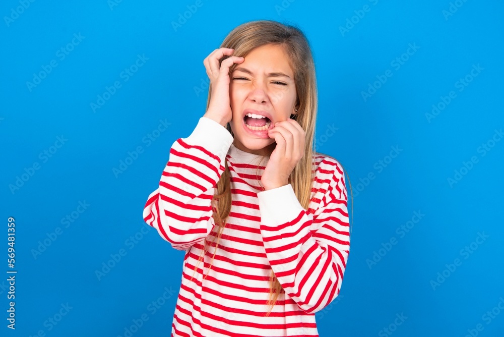 Young gloomy caucasian teen girl wearing striped shirt over blue studio ...