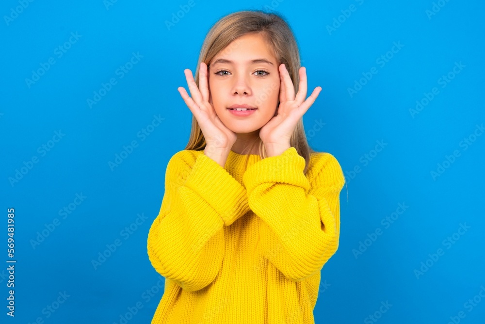 Happy caucasian teen girl wearing yellow sweater over blue studio ...