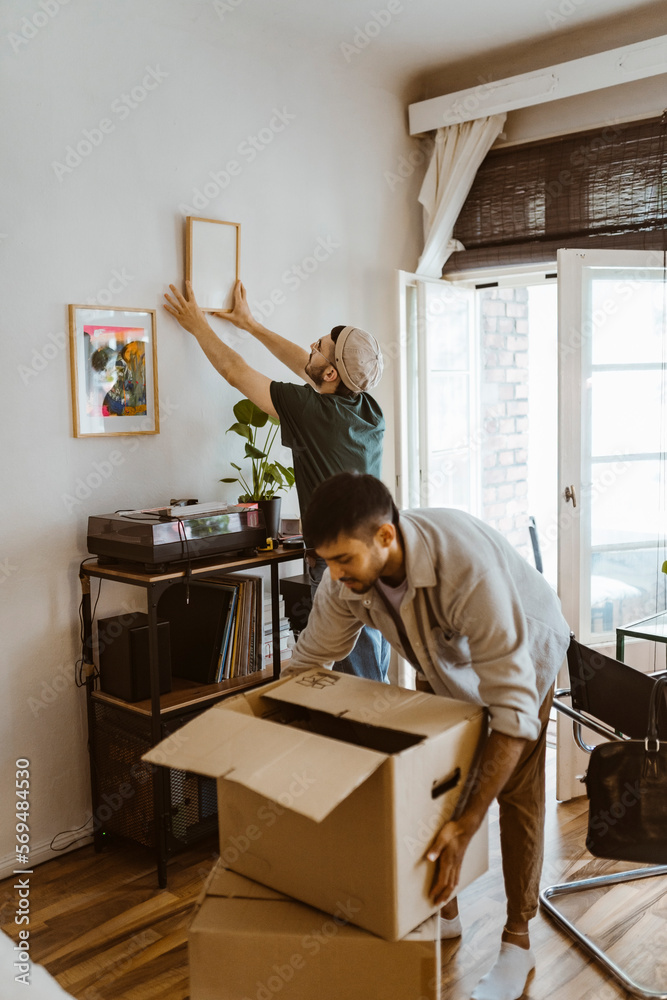 Man mounting frame on wall with boyfriend stacking cardboard boxes at ...