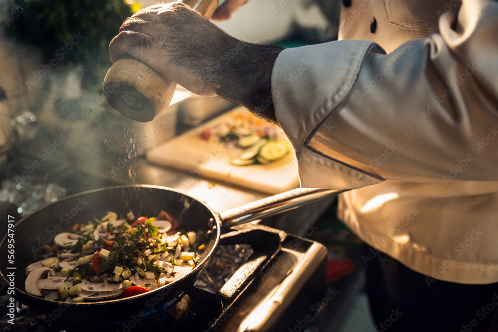 Chef cooking in a commercial kitchen puts the spice on the dish. Stock ...