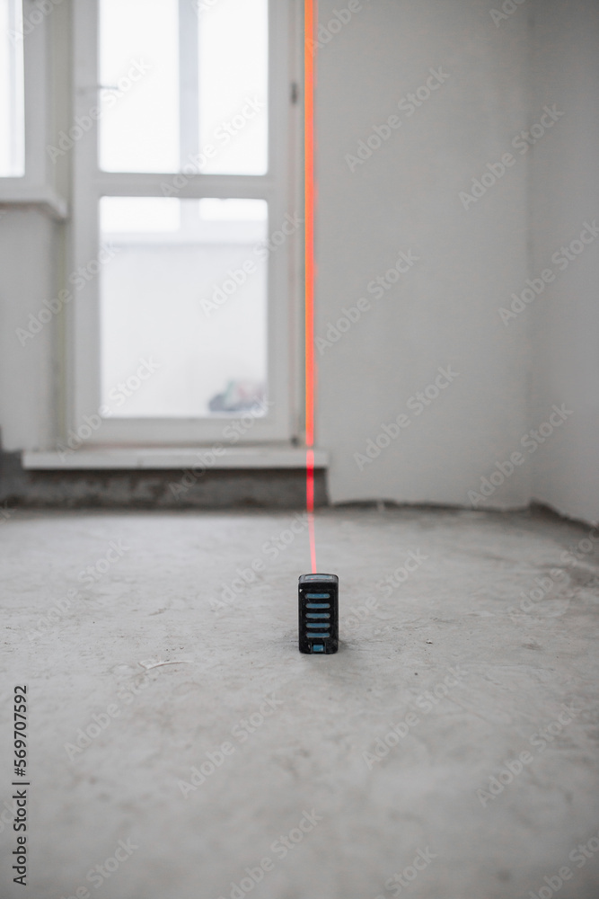 The laser level on the floor in an empty room draws a vertical line to ...