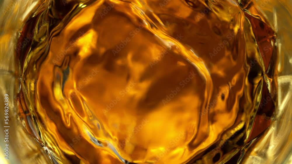 Super Slow Motion Detail Shot of Golden Alcohol Liquid Waving in Glass ...