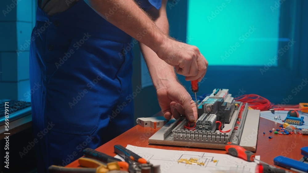 Unrecognizable man with a screwdriver in his hands twists the red wire ...