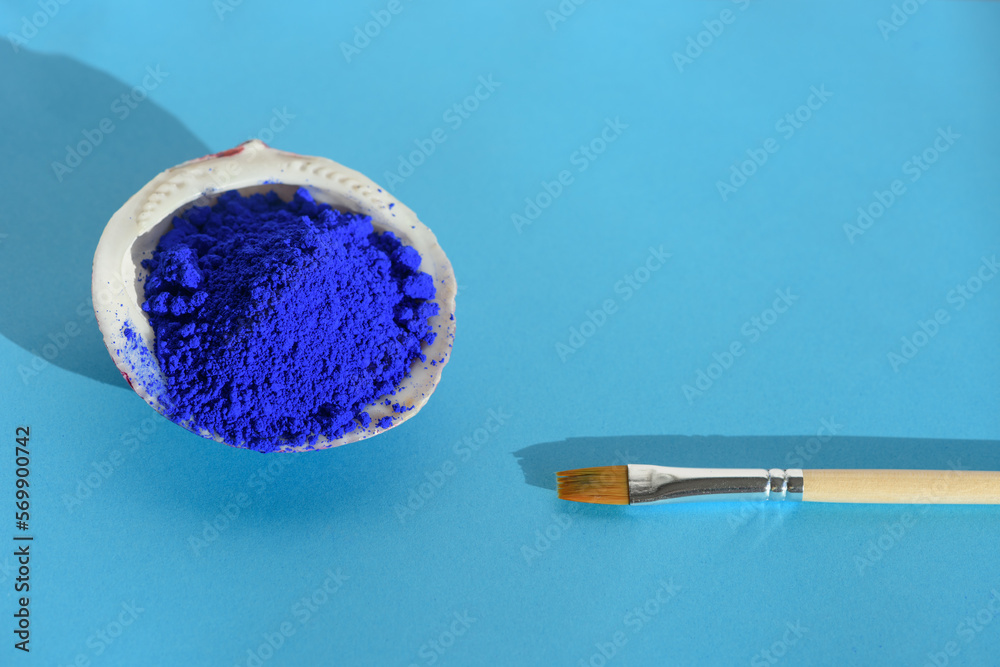 Pigmento azul en una concha y pincel sobre fondo azul intenso. Plano ...