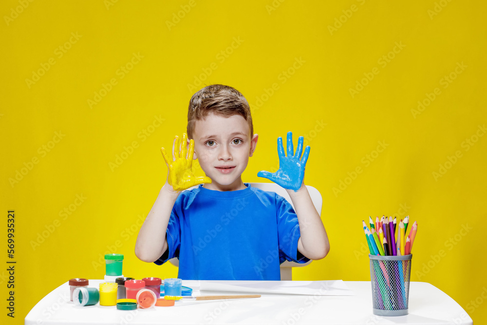 A little preschooler is sitting at a table, drawing with his palms on a ...