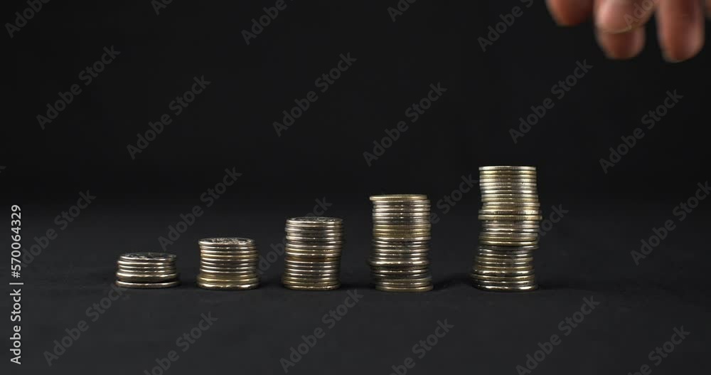 A man's hand on a black background stacks coins. Stacks of coins stand ...