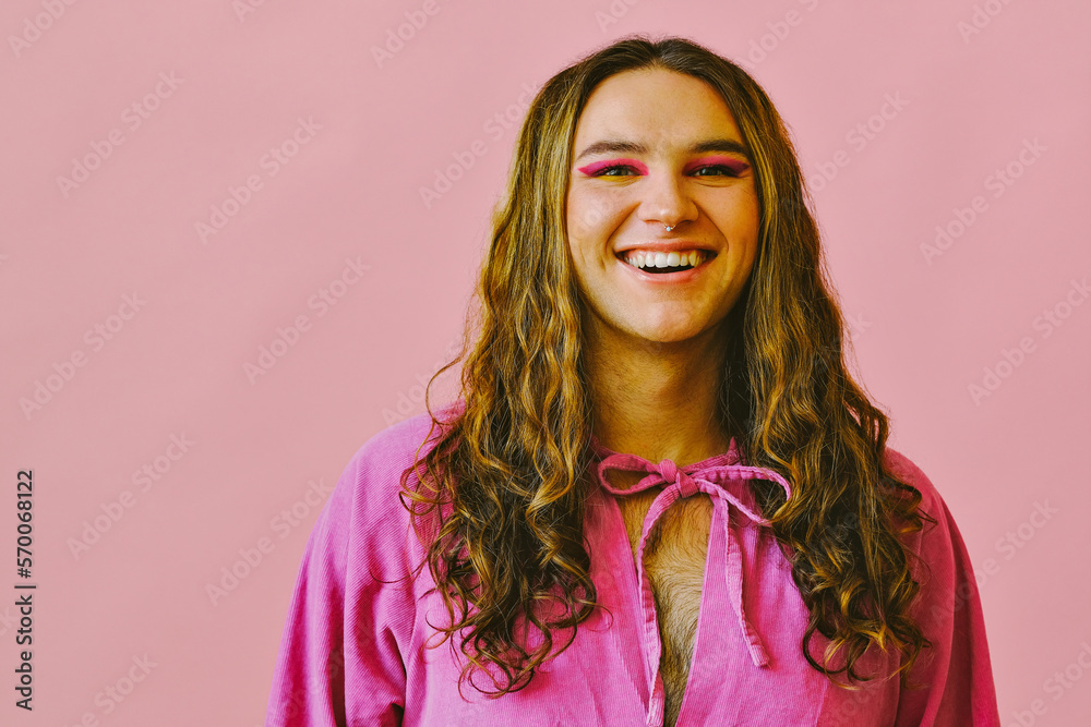 Non-binary adult with long wavy hair smiling against pink background ...