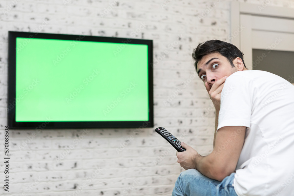 Shocked man on the couch watching tv. Bad news and Green screen concept ...