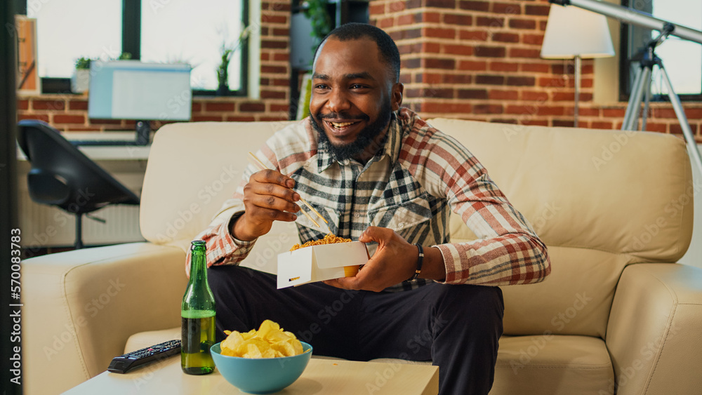 African american man enjoying asian food in delivery box, using ...