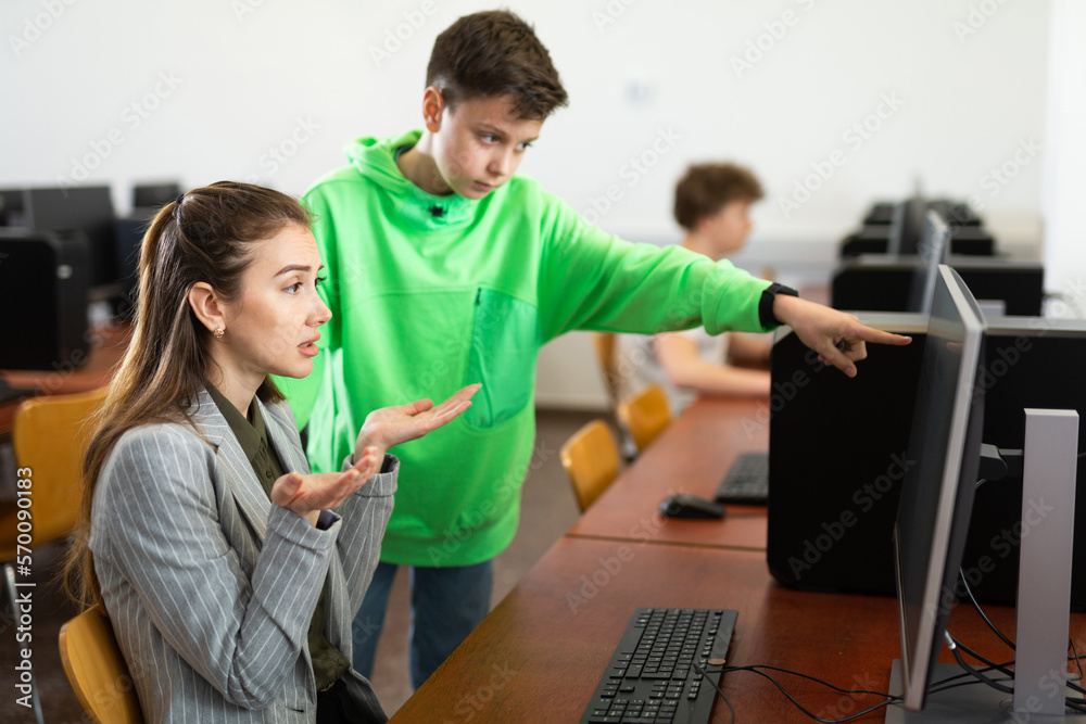 Female teacher and teenage boy trying to solve computer problem during ...