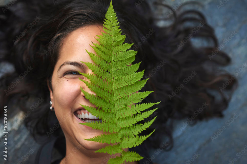 Woman with a fern on her face. She's lying on a rock and covers half ...