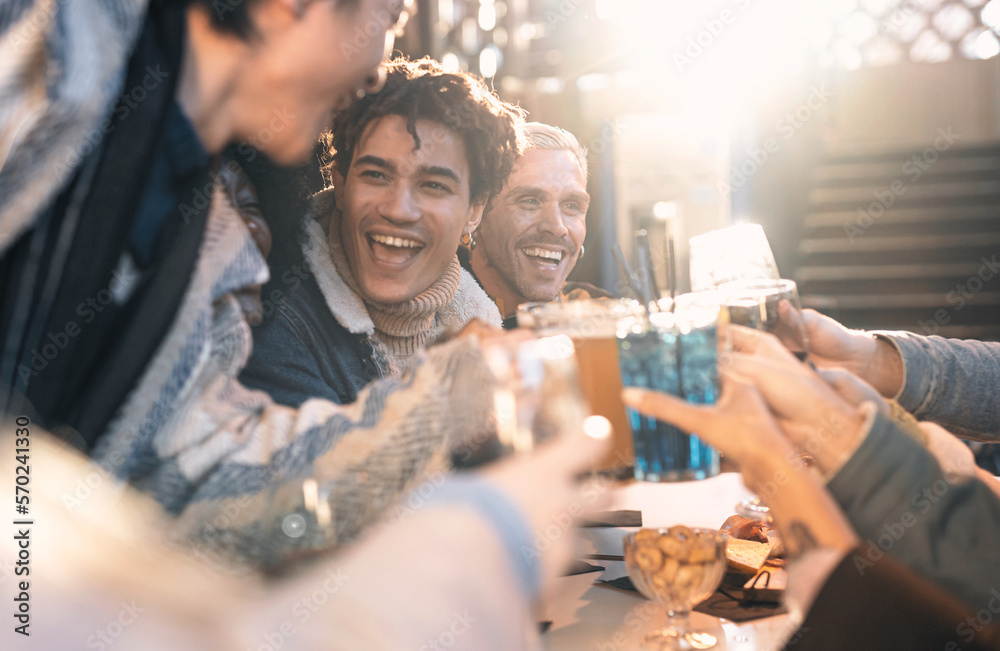 A group of grinning friends gather around a bar table, raising their ...