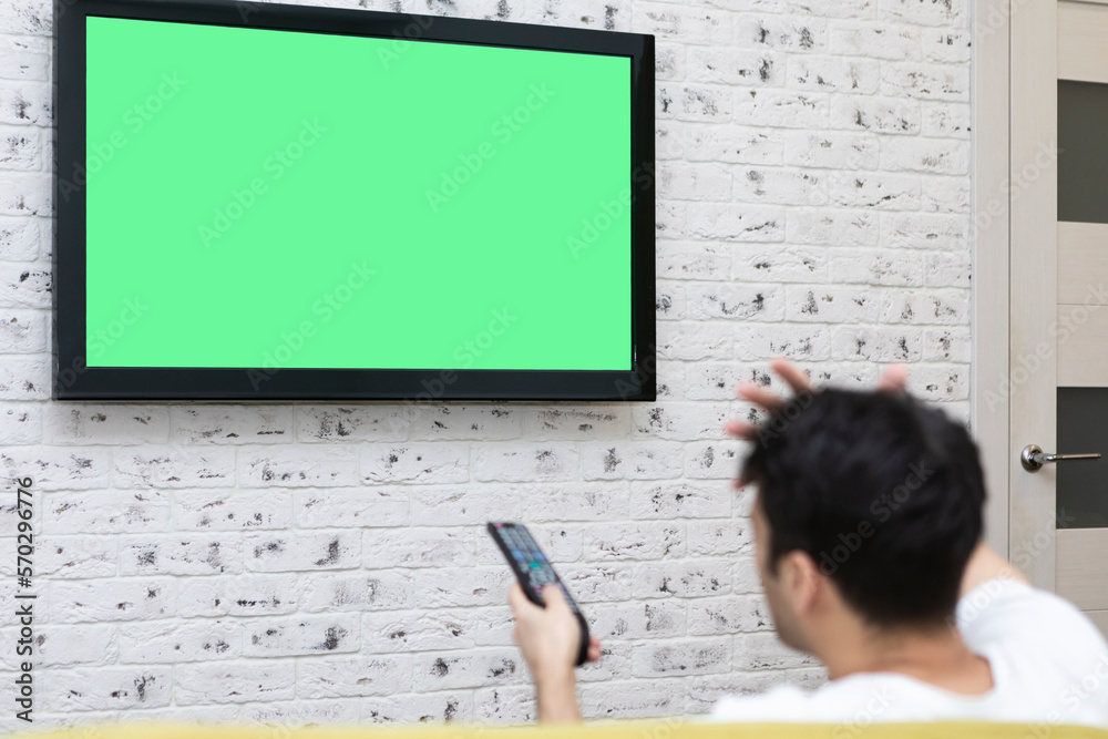 Fototapeta Shocked man on the couch watching tv. Bad news and Green ... Fototapeta Shocked man on the couch watching tv. Bad news and Green ...