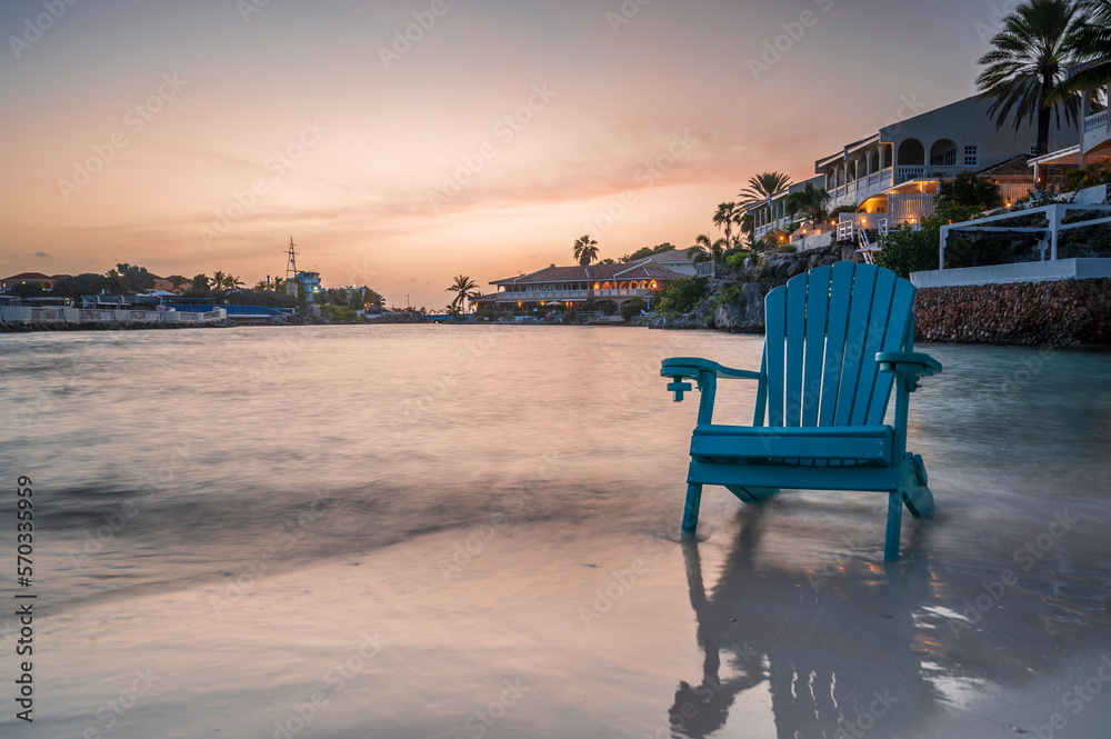 An Adirondack chair, on the shoreline of a tropical beach, at sunset ...