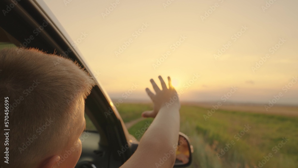 Boy stretches out his hand from car window catch sun glare of sunset ...
