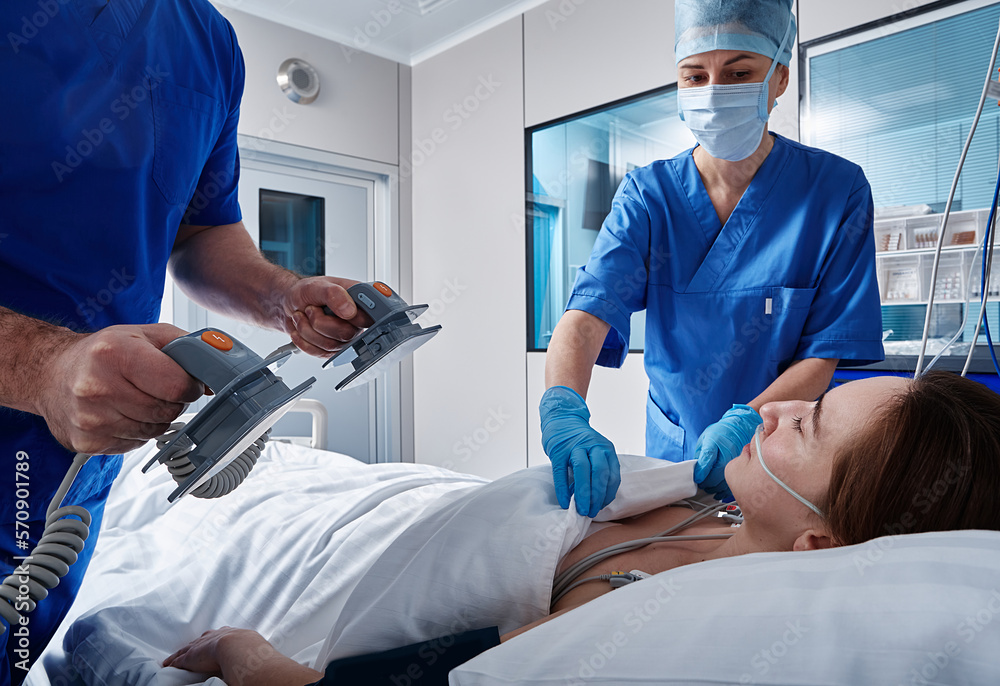 Medical team performing a reanimation with defibrillator on unconscious woman patient lying on ...