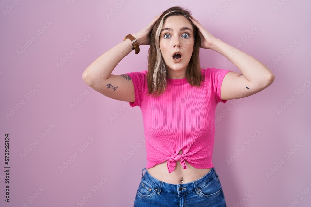 Blonde caucasian woman standing over pink background crazy and scared ...