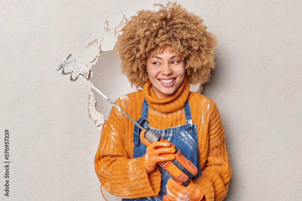 Cheerful female plasterer holds mixer for mixing plaster on walls wears ...