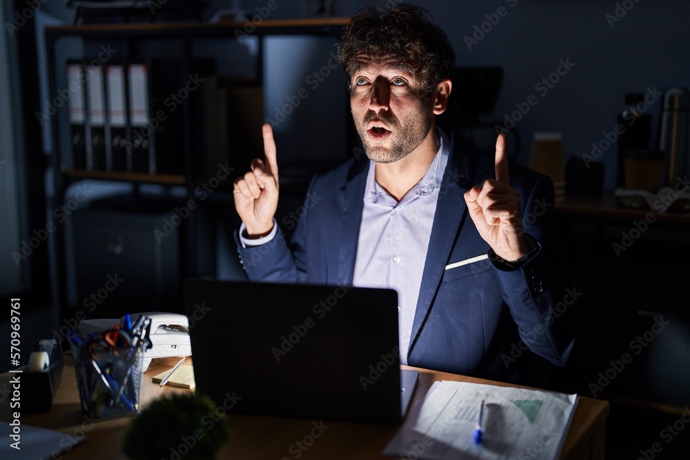 Hispanic young man working at the office at night amazed and surprised ...