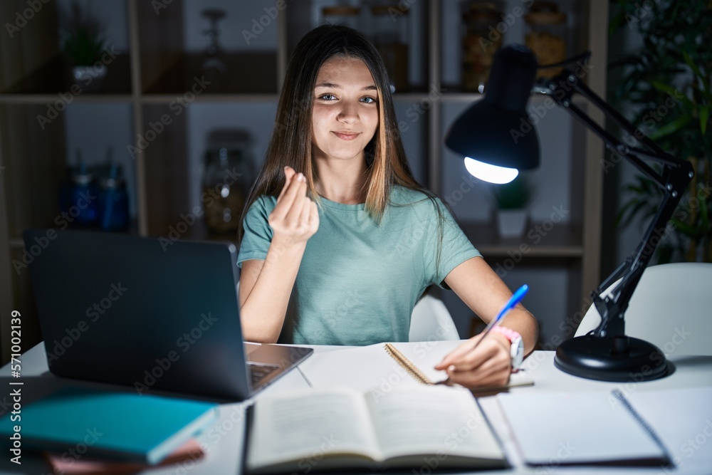 Teenager girl doing homework at home late at night doing money gesture ...