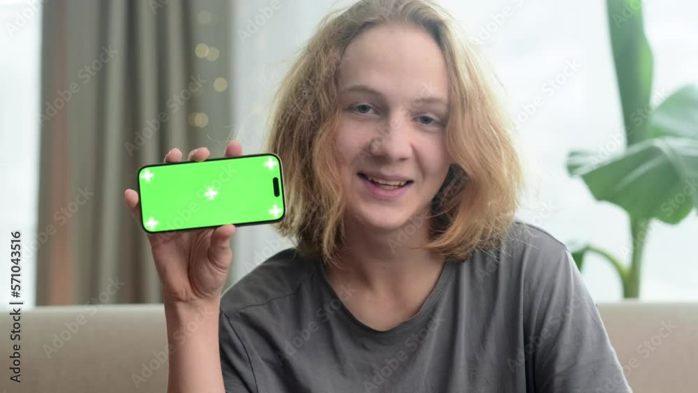 smiling ginger long hair teen boy showing horizontal phone with green ...