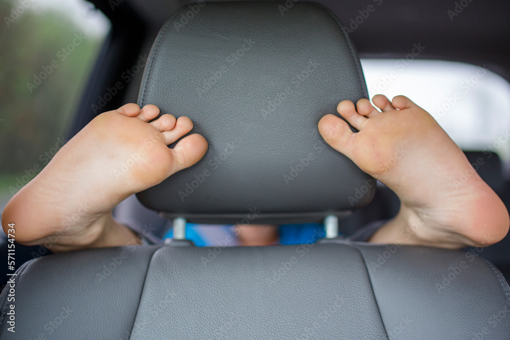 A child in the backseat of a car wraps his feet round the front seat ...
