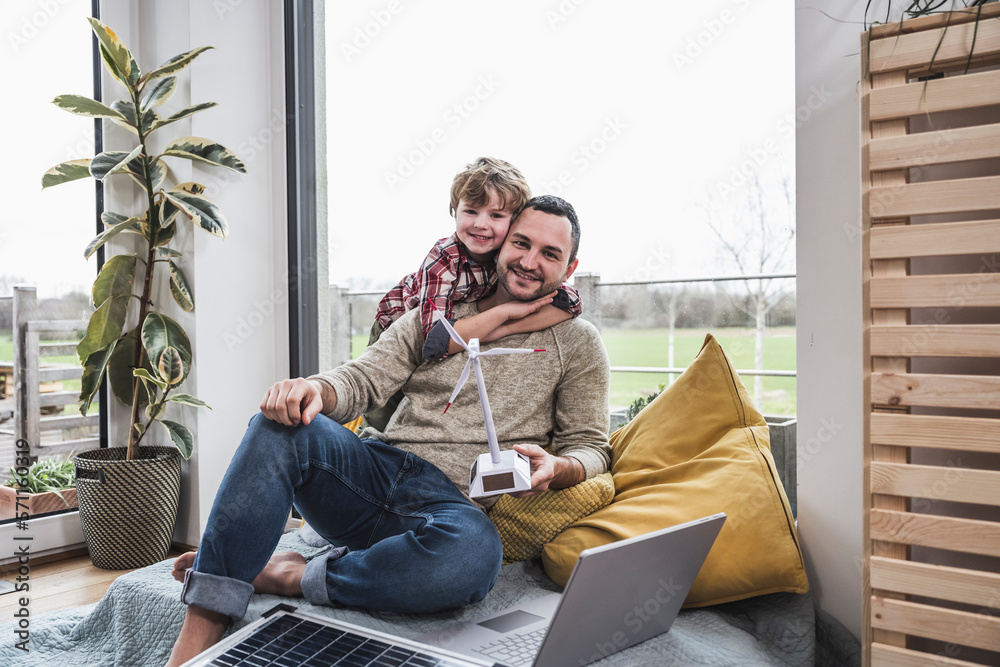 Happy father holding wind turbine model with son embracing from behind ...