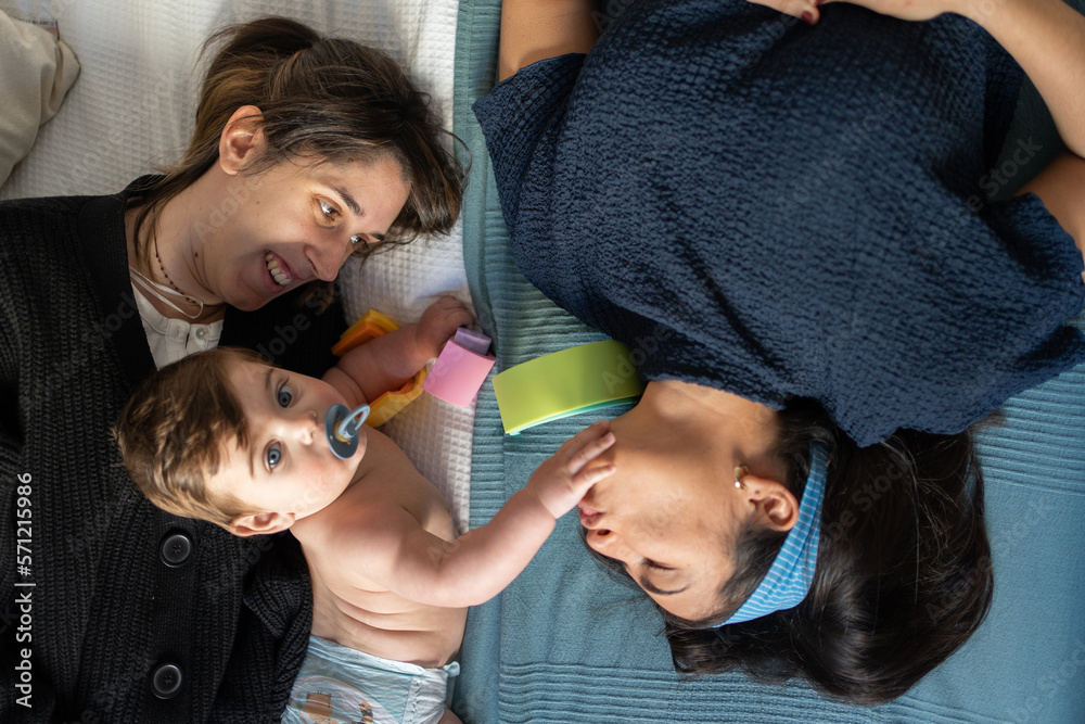 two mothers with baby in bed laughing and playing with montessori ...
