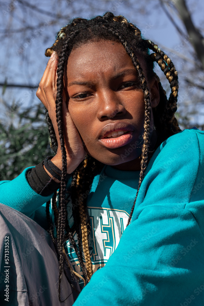 Mujer joven de color con trenzas y sudadera sentada en un parque de ...