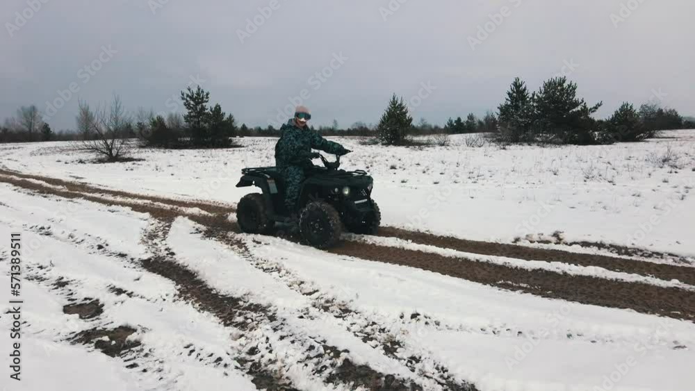 Woman riding on an ATV through the snowy landscape, side view. Quad ...