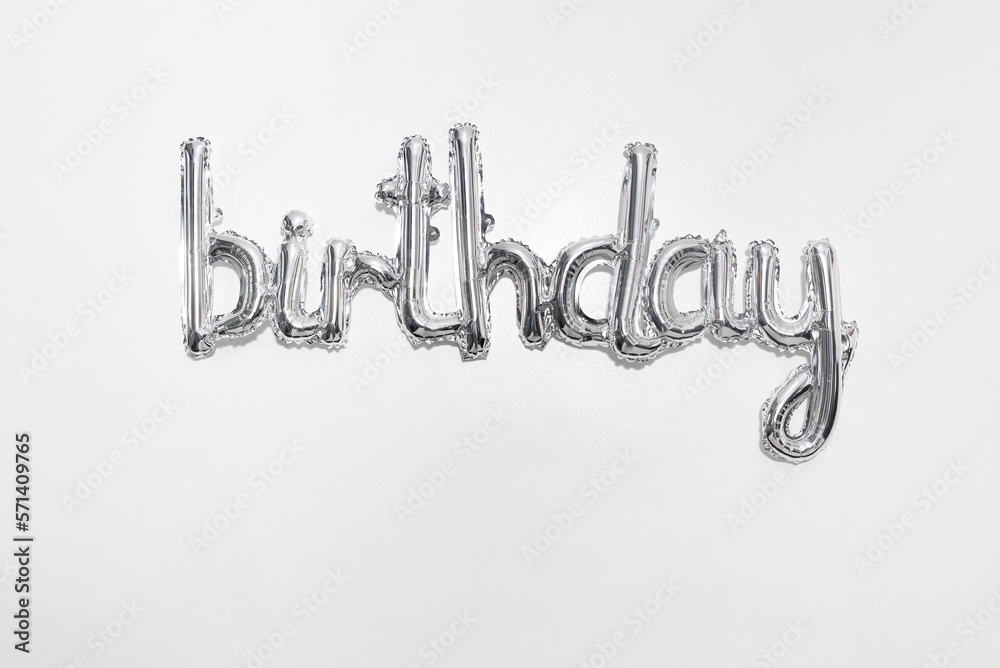 Silver birthday balloon lettering center on a white wall. Foil letters ...