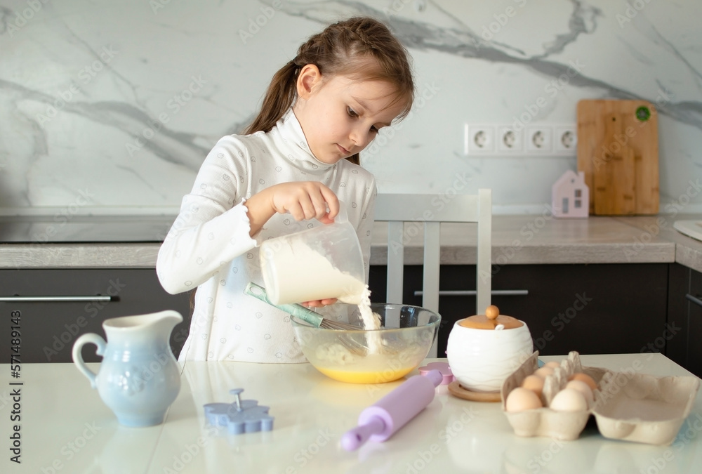 Charming 7-year-old girl is learning to cook in white kitchen. Happy ...