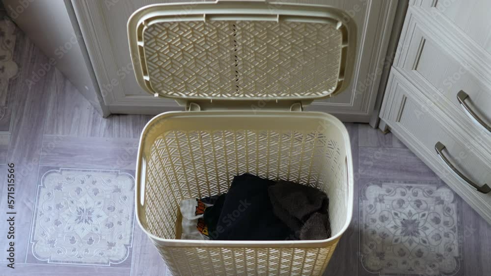 child's hand puts clothes in the dirty laundry container for washing in ...