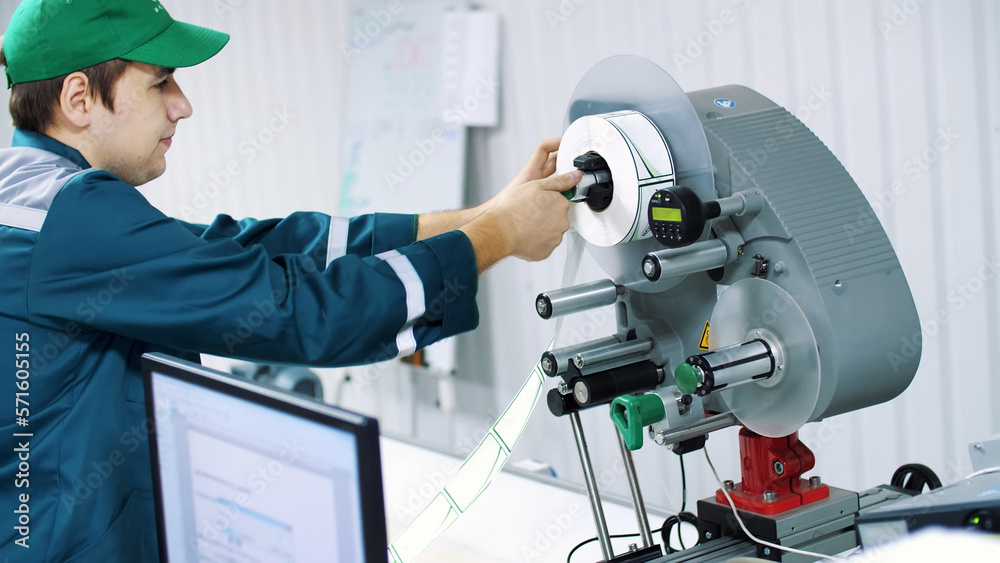 The worker changes paper roll with marking stickers on a machine with ...