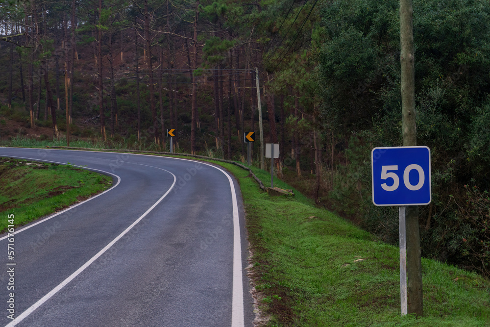 Road with a blue road sign with the number 50 among the hills covered ...