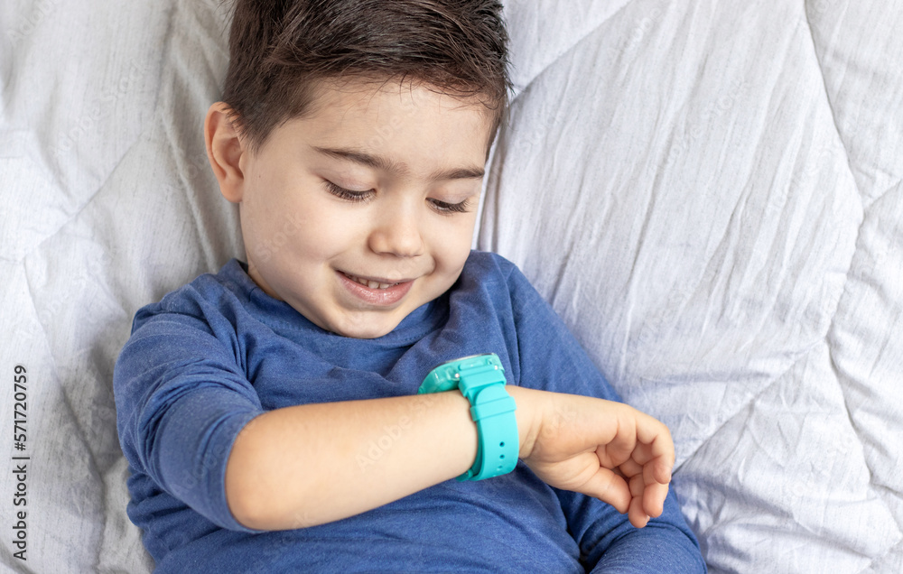 cute adorable kid using smartwatch lies lying on bed.happy child ...