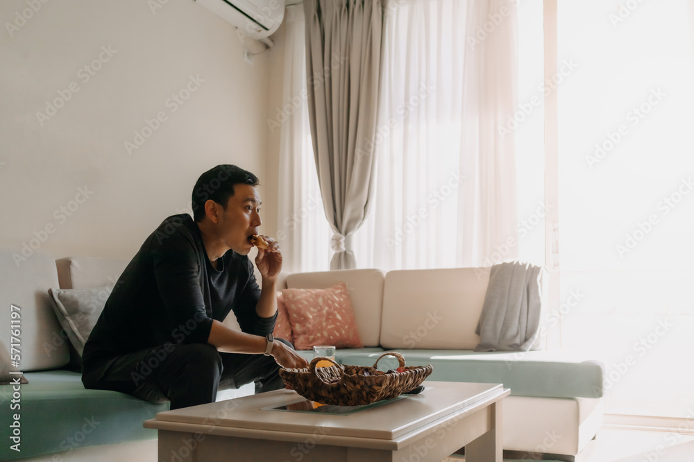 Asian man having bread and juice as breakfast on the sofa living room ...