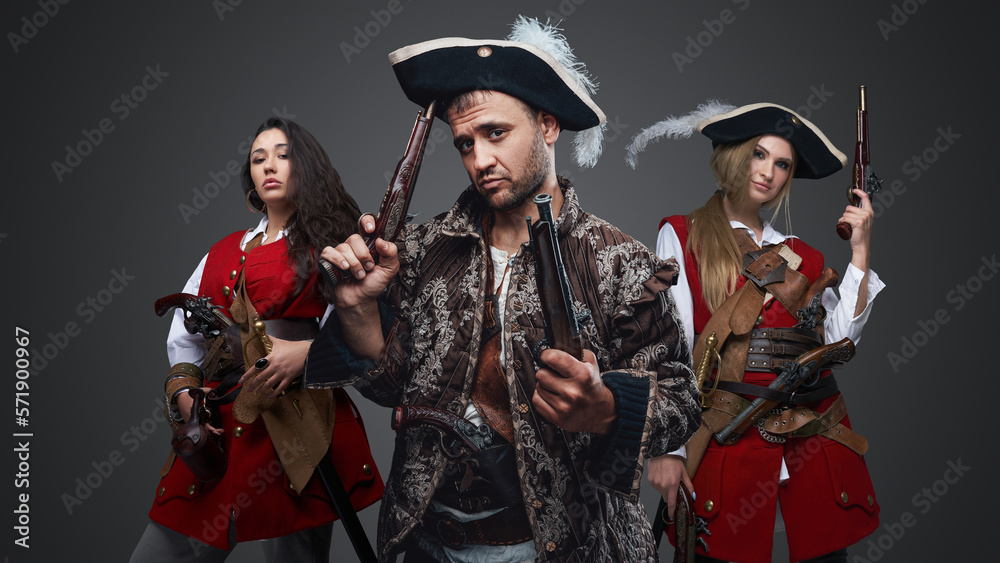 Shot of pirate man and two women with flintlock guns against grey ...