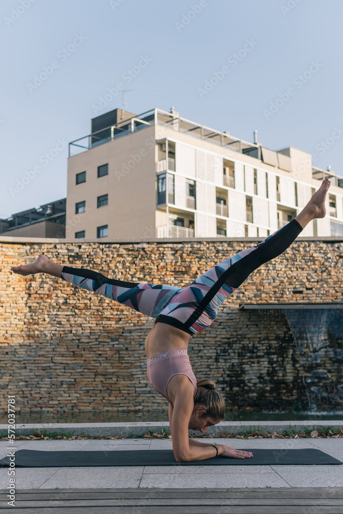 Vertical shot of a young woman performing yoga outdoors on her mat ...