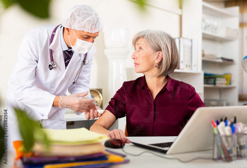 Elderly female office employee receiving injection from qualified ...