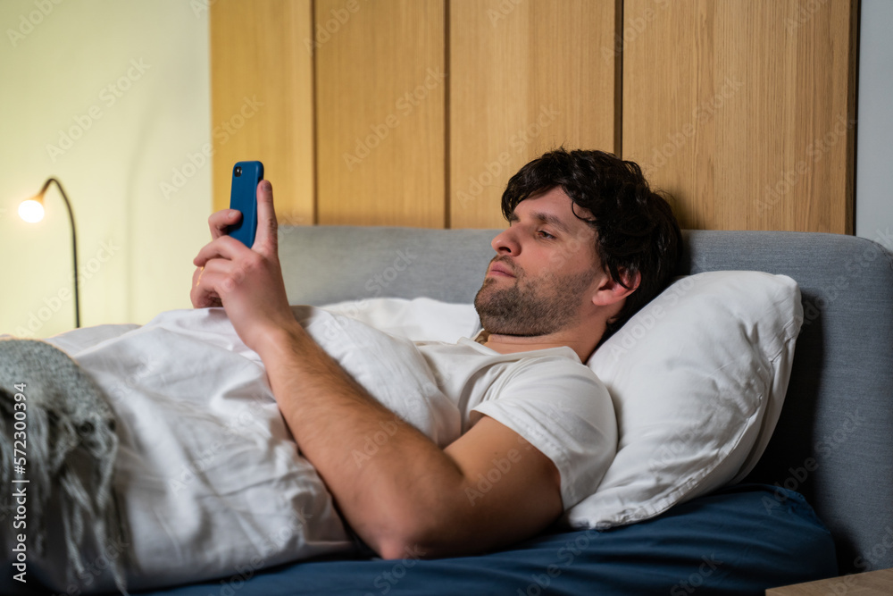 Insomnia and mobile phones. A man is lying on a bed and using a ...