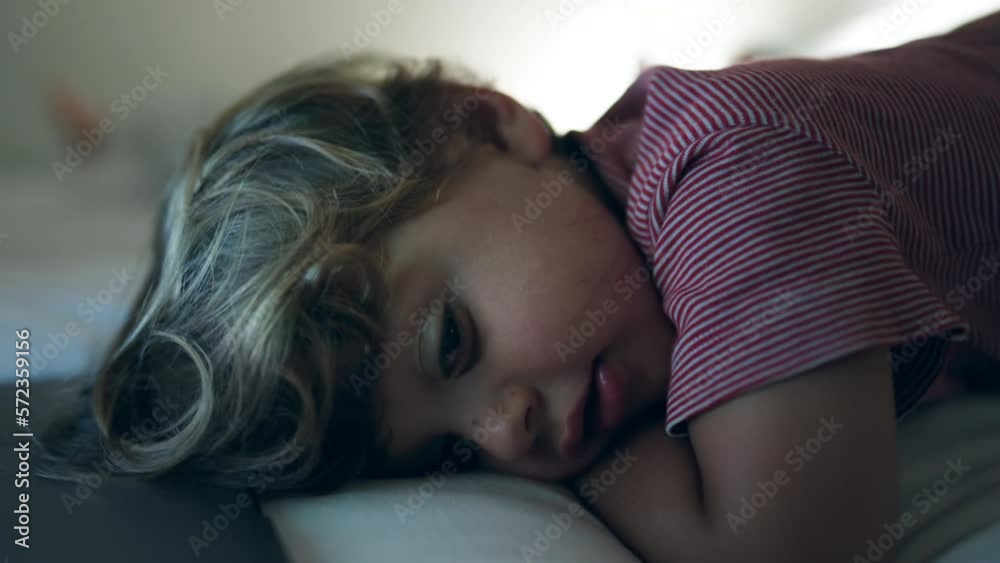 Child watching cartoons laying in bed hypnotized by screen at night ...