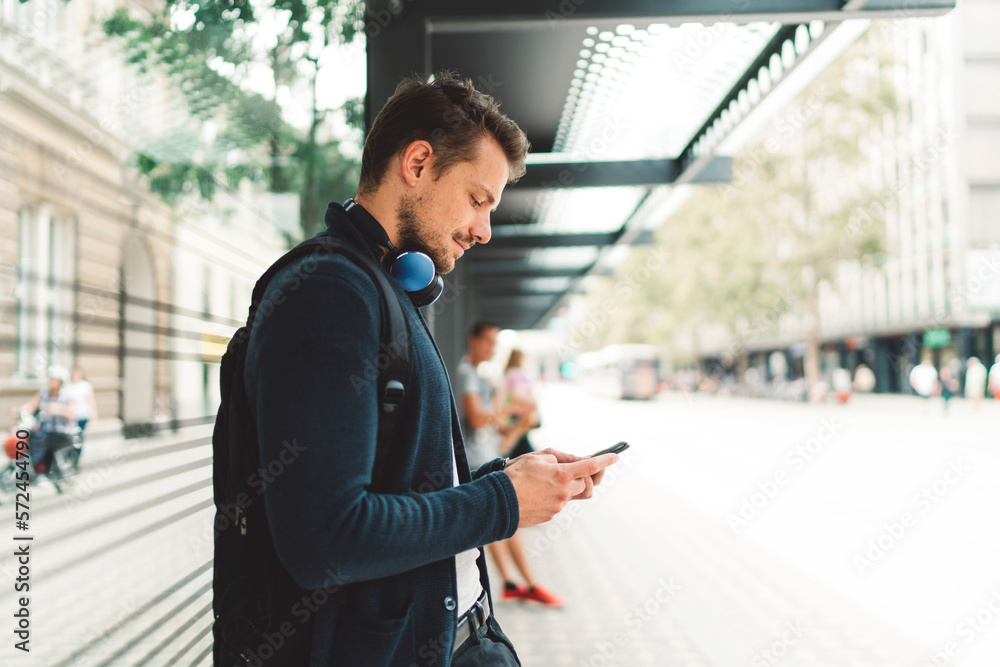 Side view of young man looking down at his phone while waiting for his ...