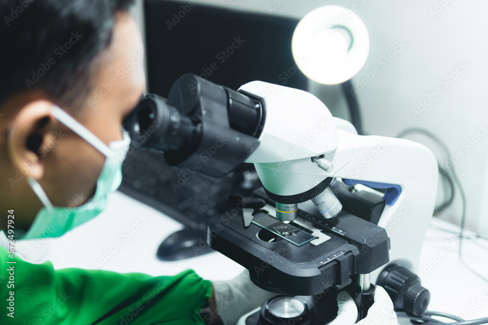 Scientist Looking Under Microscope, Wearing Green Protective Clothing ...